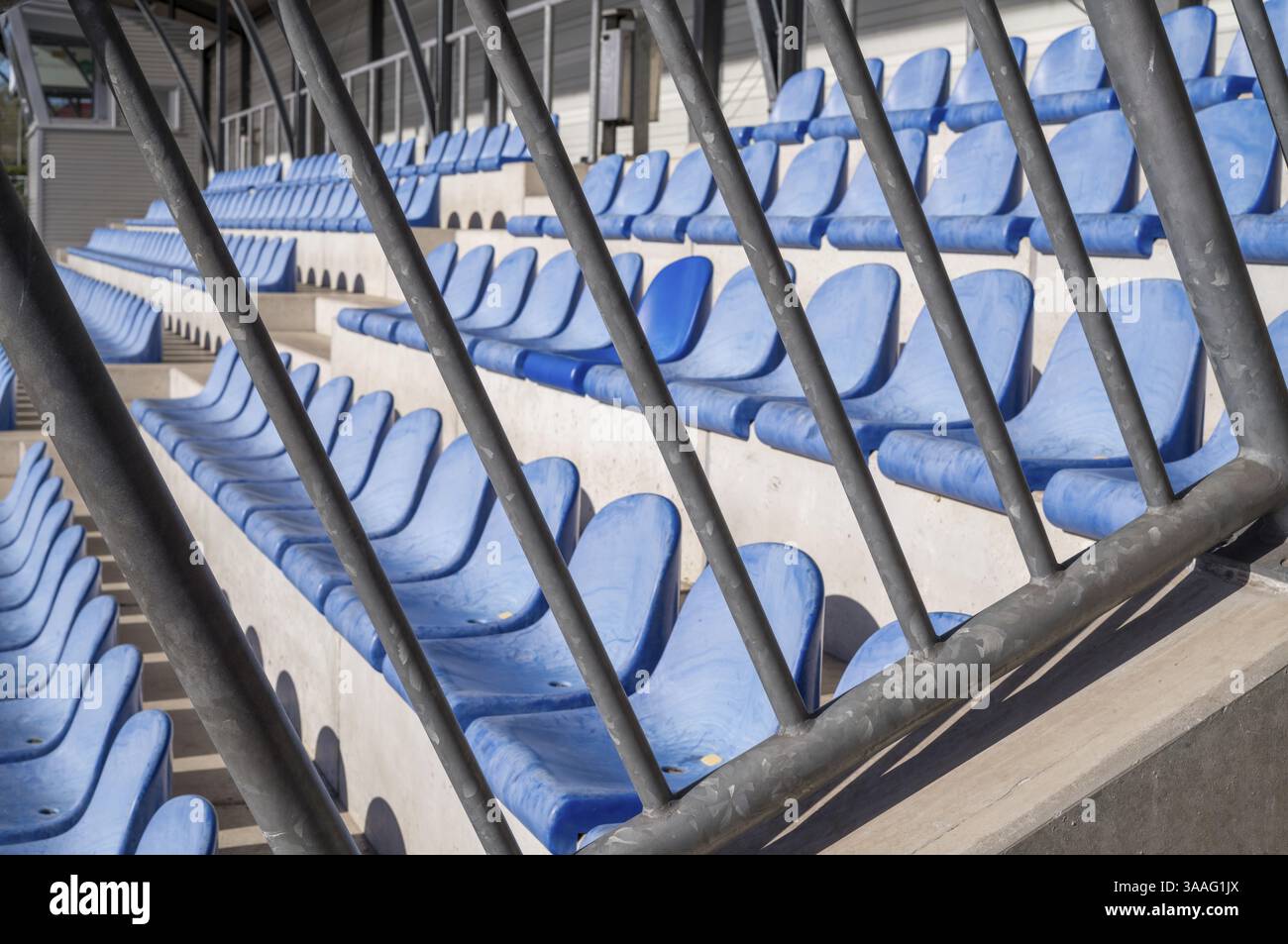 Rows of empty blue plastic stadium seats behind a metal barrier await ...