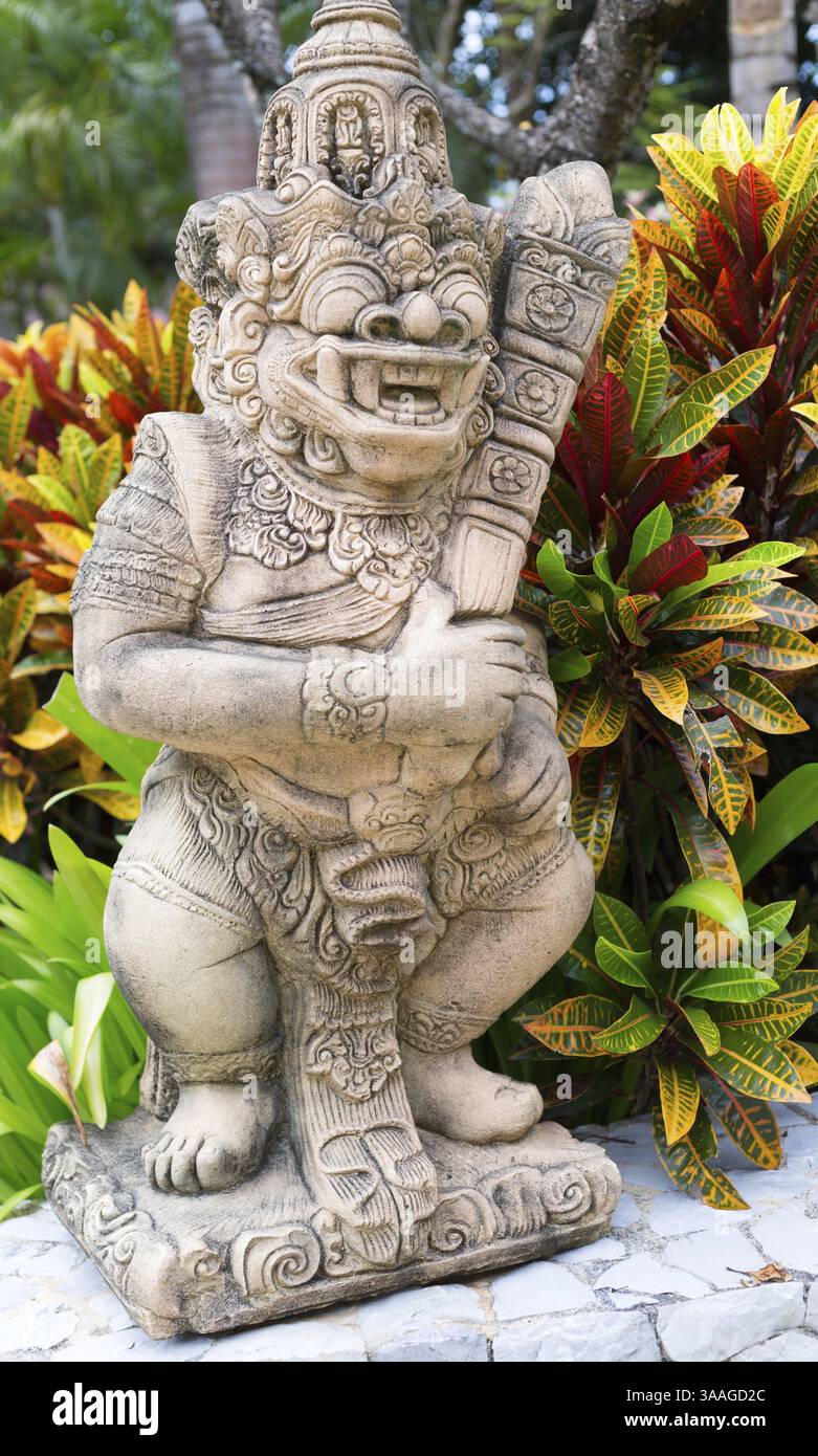 Thai stone god in the bushes of tropical plants. Short depth of field ...