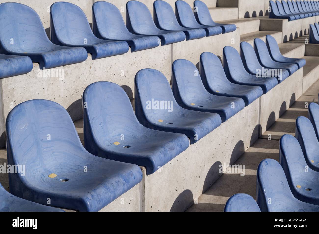 Rows of empty blue plastic seats casting shadows on concrete steps in a ...