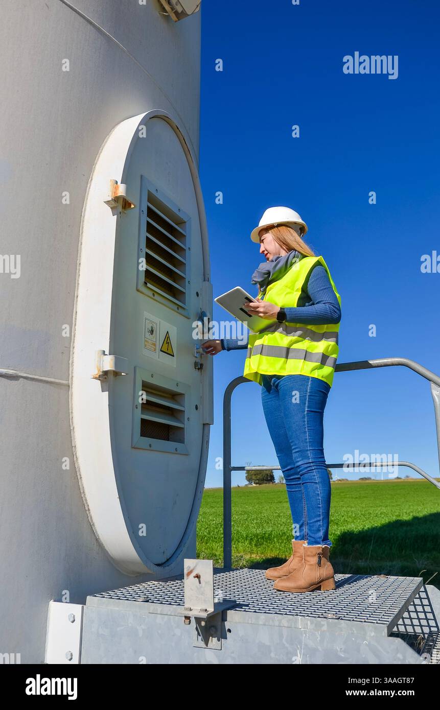 Female engineer wearing safety vest and helmet working at wind turbine ...