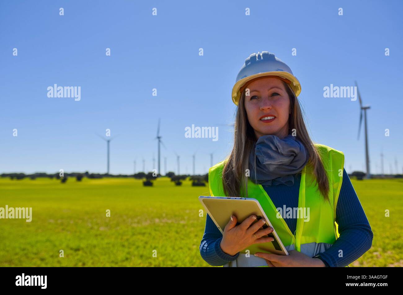 Confident female engineer holding tablet inspecting wind turbine farm ...