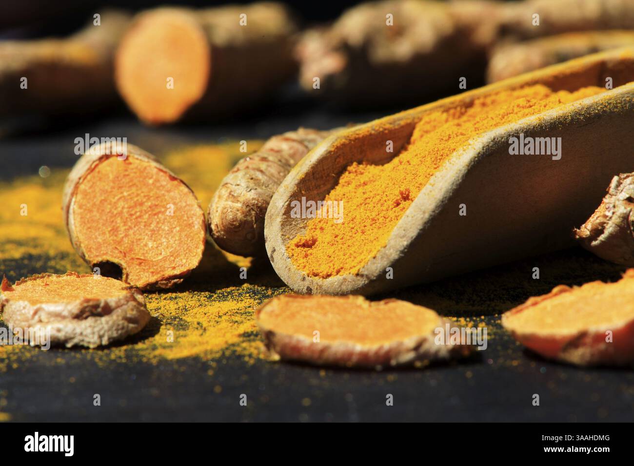 Turmeric powder (curcuma) in a wooden spoon and roots on a dark table ...