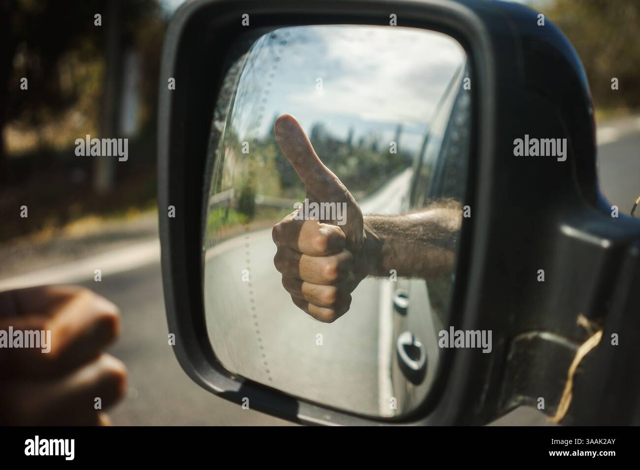 Thumbs up greeting, reflection in the rear-view mirror of a car on the ...
