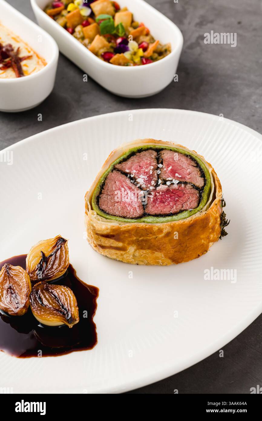 Modern plate of Beef Wellington, caramelized shallots and dark sauce ...