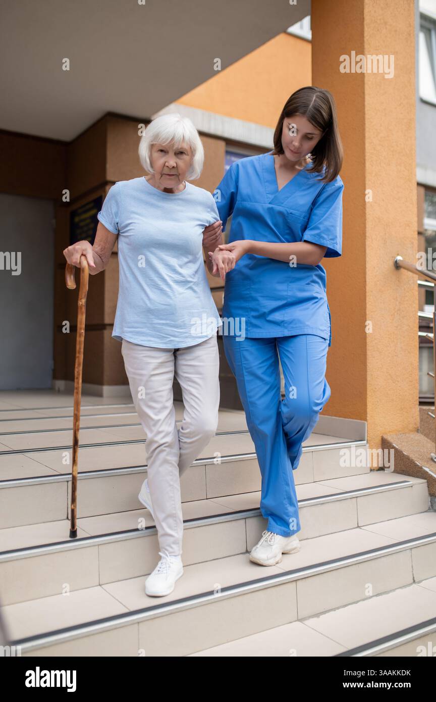 Medical worker helping elderly patient with walking stick Stock Photo ...