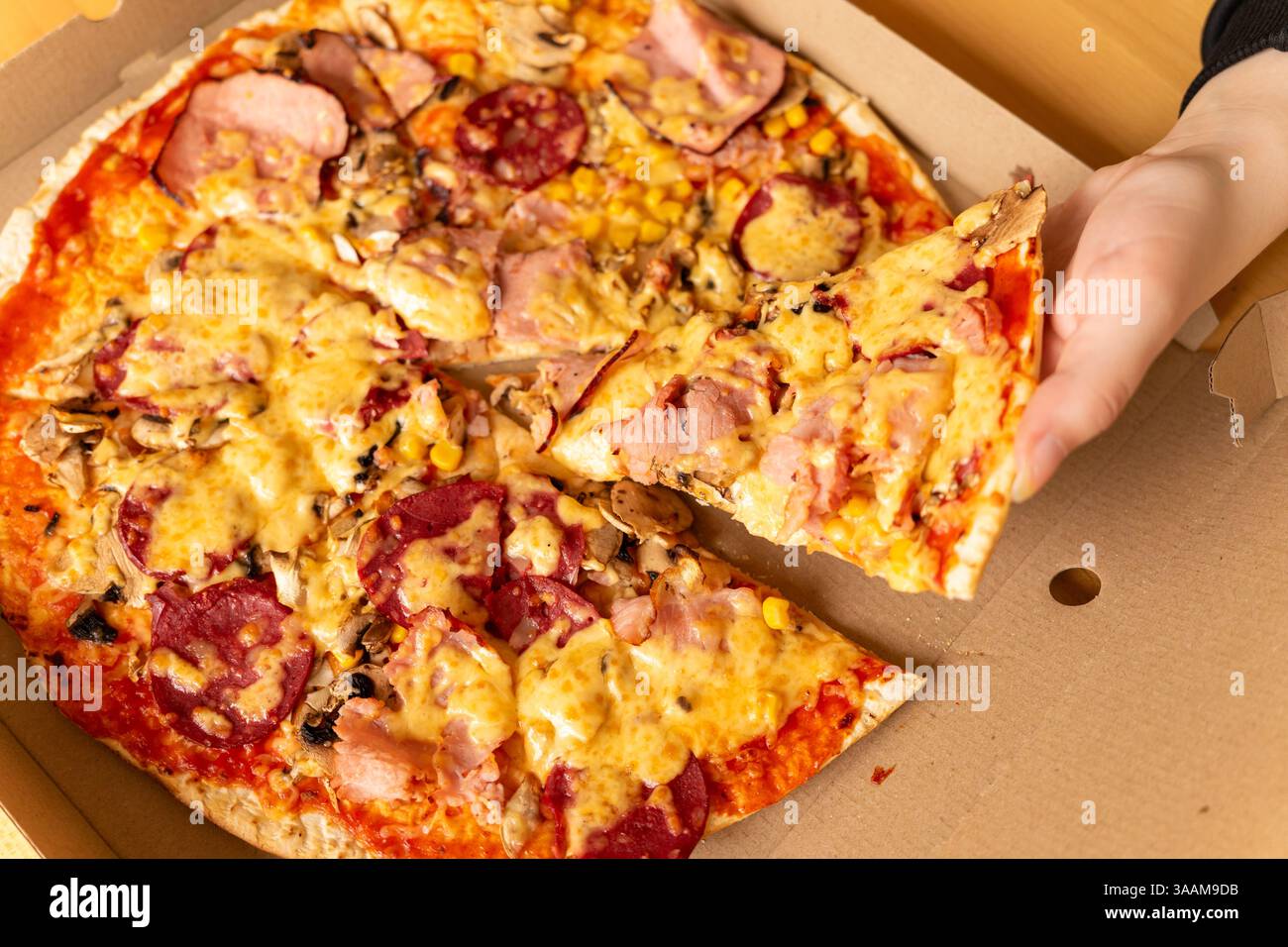 A person reaches for a slice of pizza from a takeout box. The pizza is ...