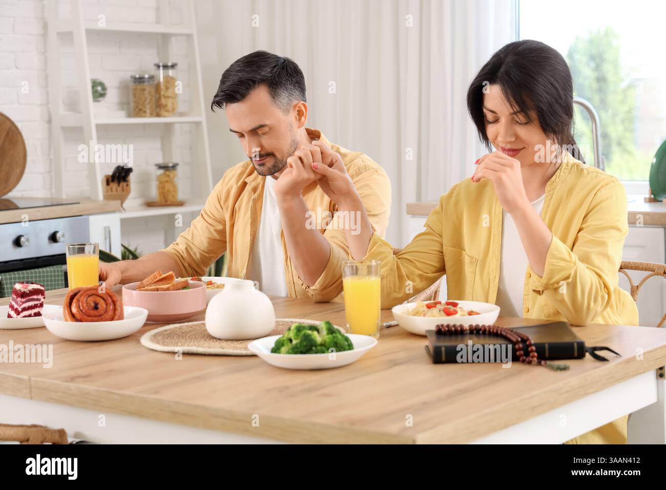 Religious couple praying before dinner at table in kitchen Stock Photo ...