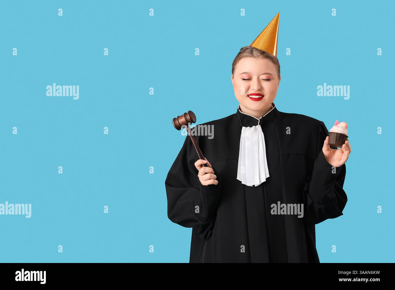 Young happy female judge in party hat with birthday cupcake and gavel ...