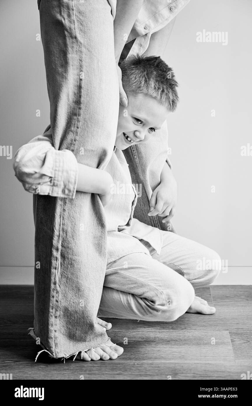 Young happy boy hugging mom's legs. Hyperactive kid holding his mother ...