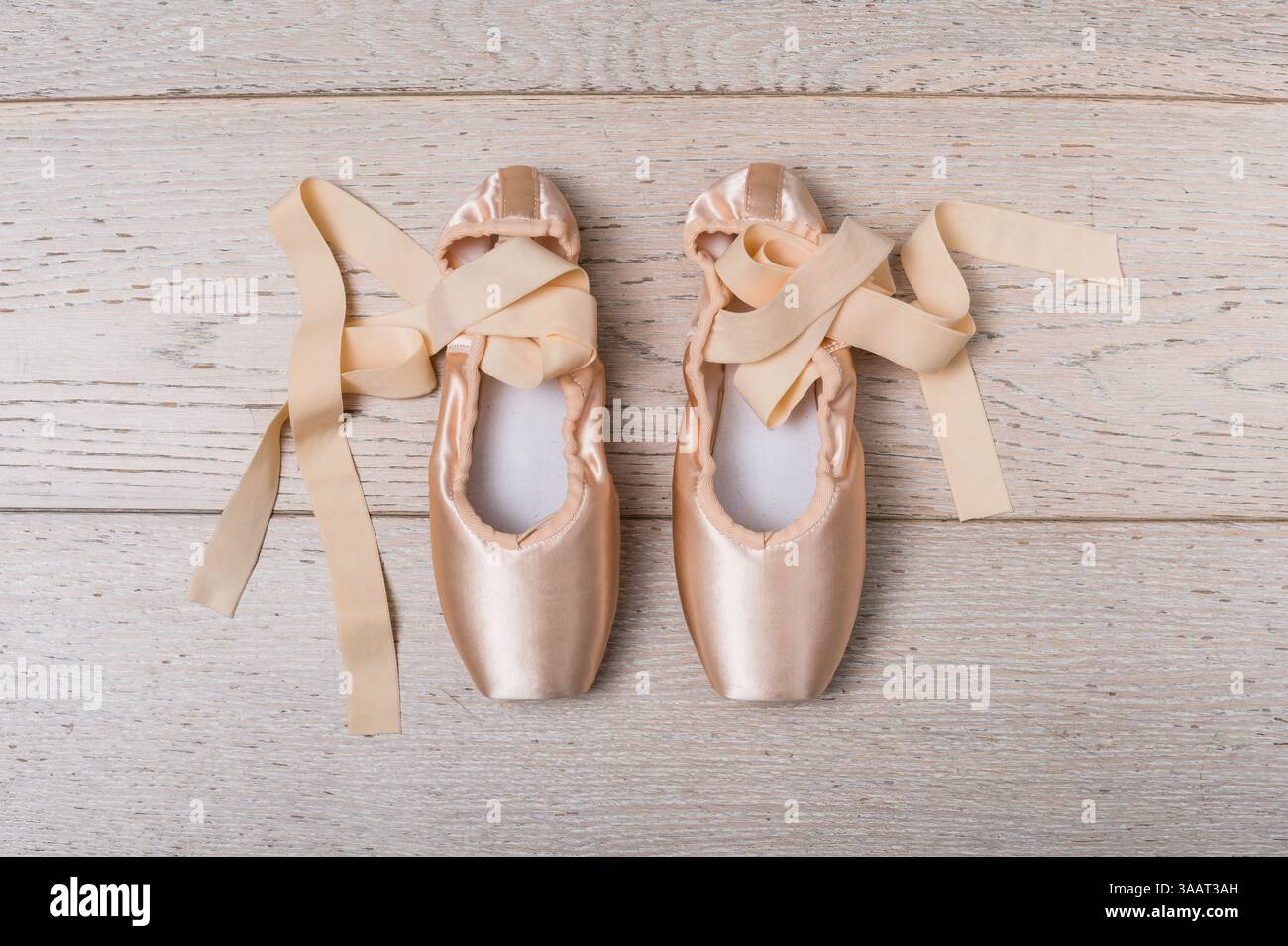 Ballet pointe shoes with satin ribbons lying on wooden floor represent ...