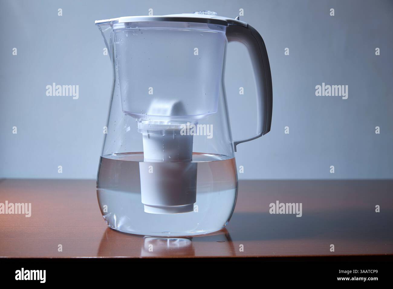 Water filter pitcher with handle filled with liquid, set on a wooden ...