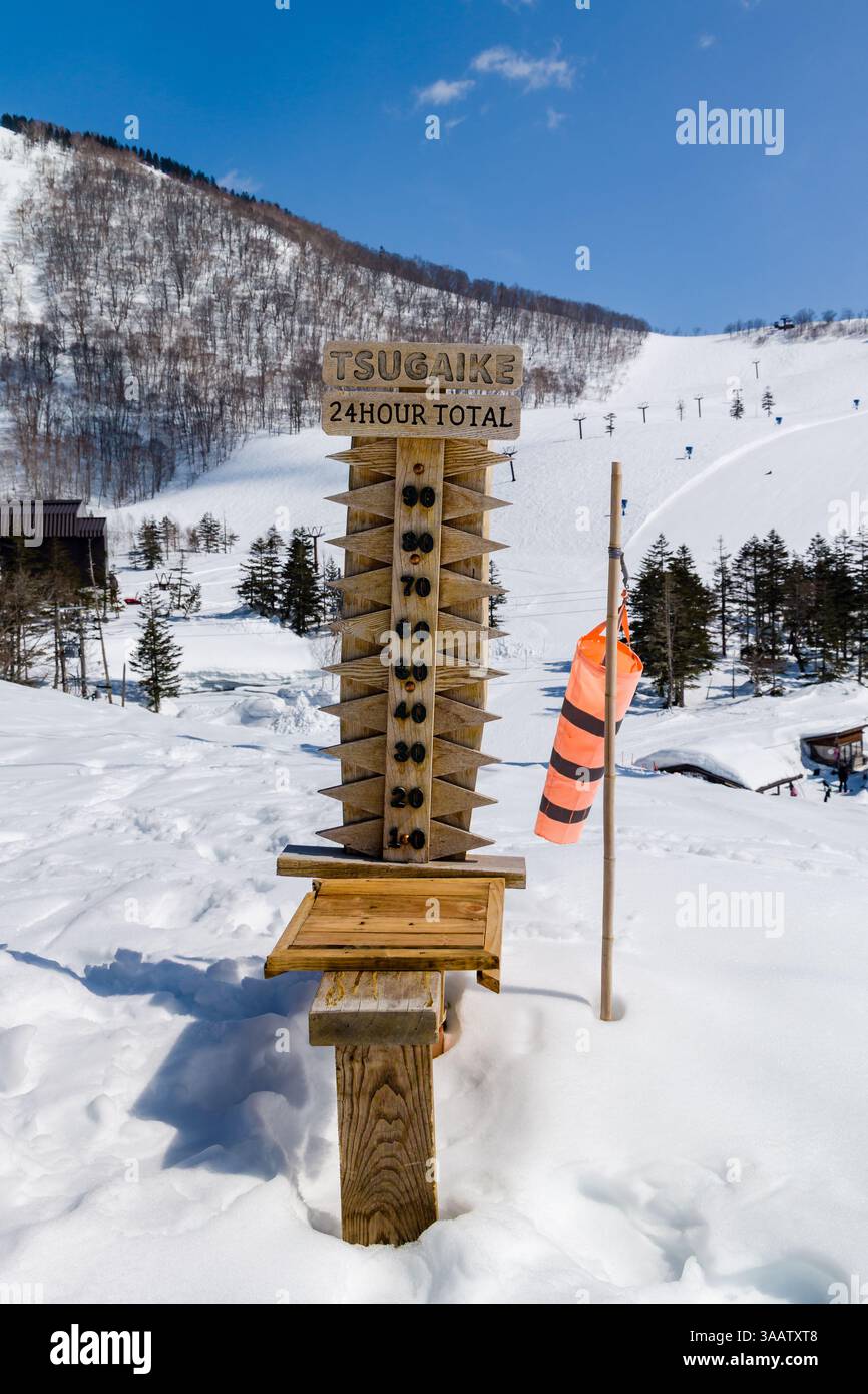 Wooden snow depth gauge at Tsugaike ski resort with a sunny ski slope ...