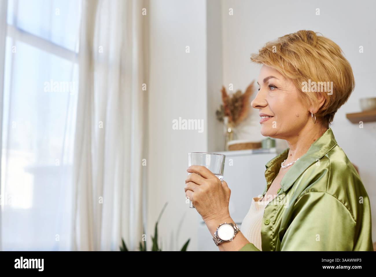 A lovely senior woman with short hair sips water, enjoying a quiet ...
