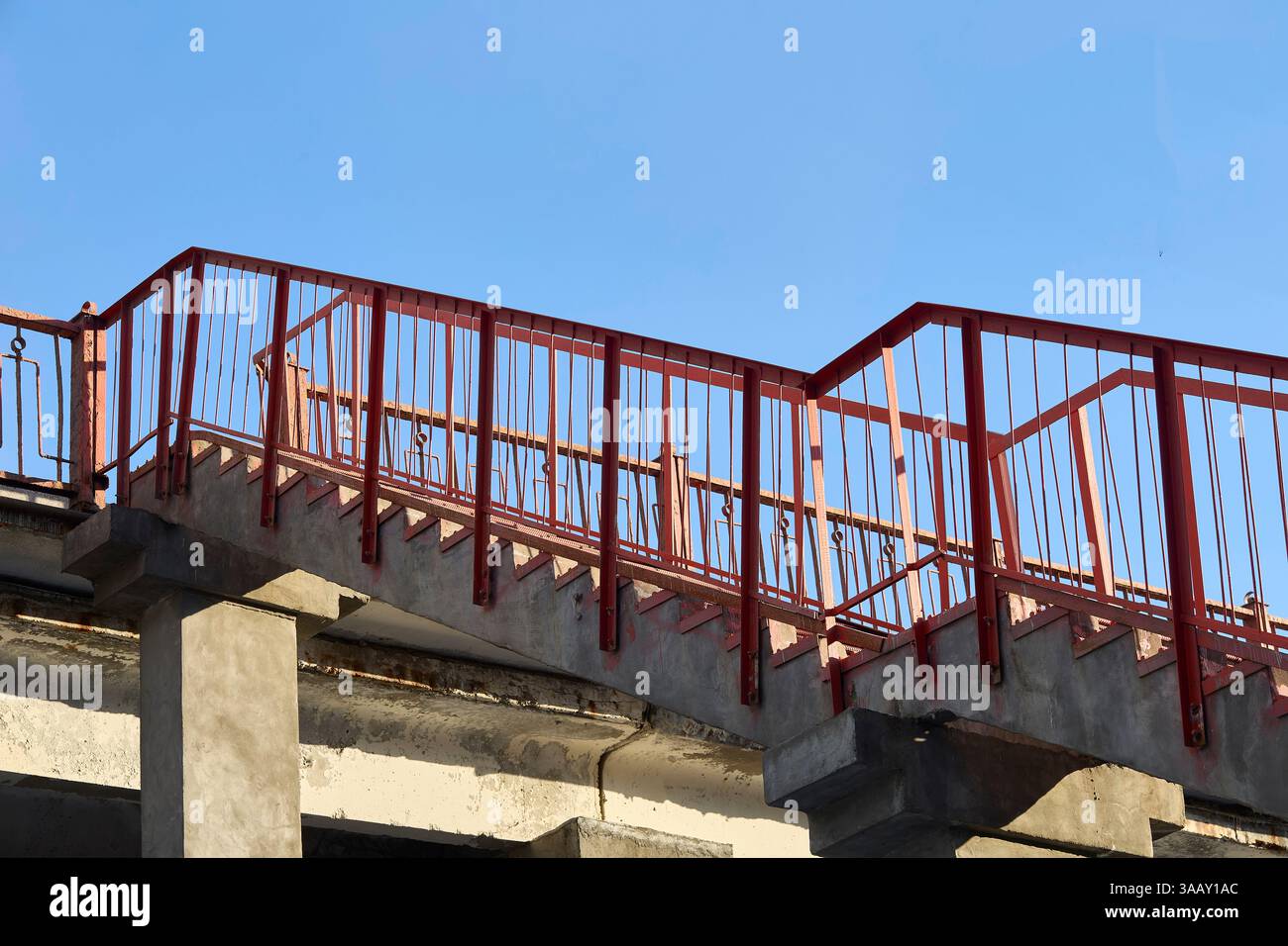 Red metal staircase leading upwards against a clear blue sky. The ...