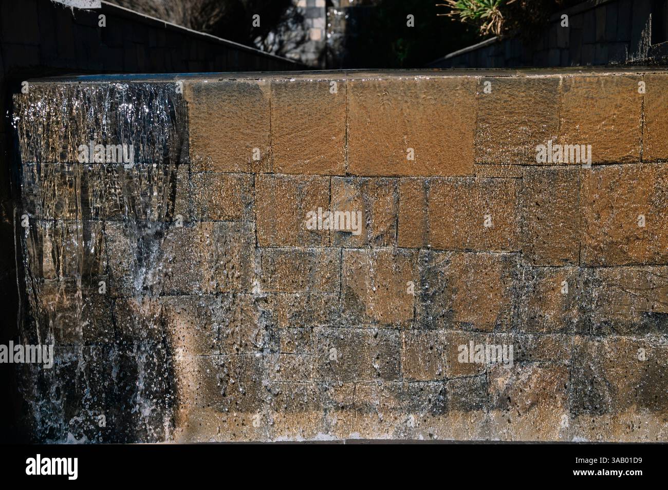 A wall with a stone wall and a water feature. The water is falling down ...
