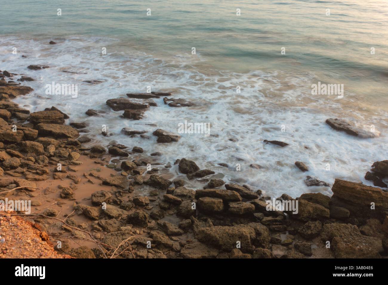 Soft ocean waves gently washing over rocks at sunset, creating a ...