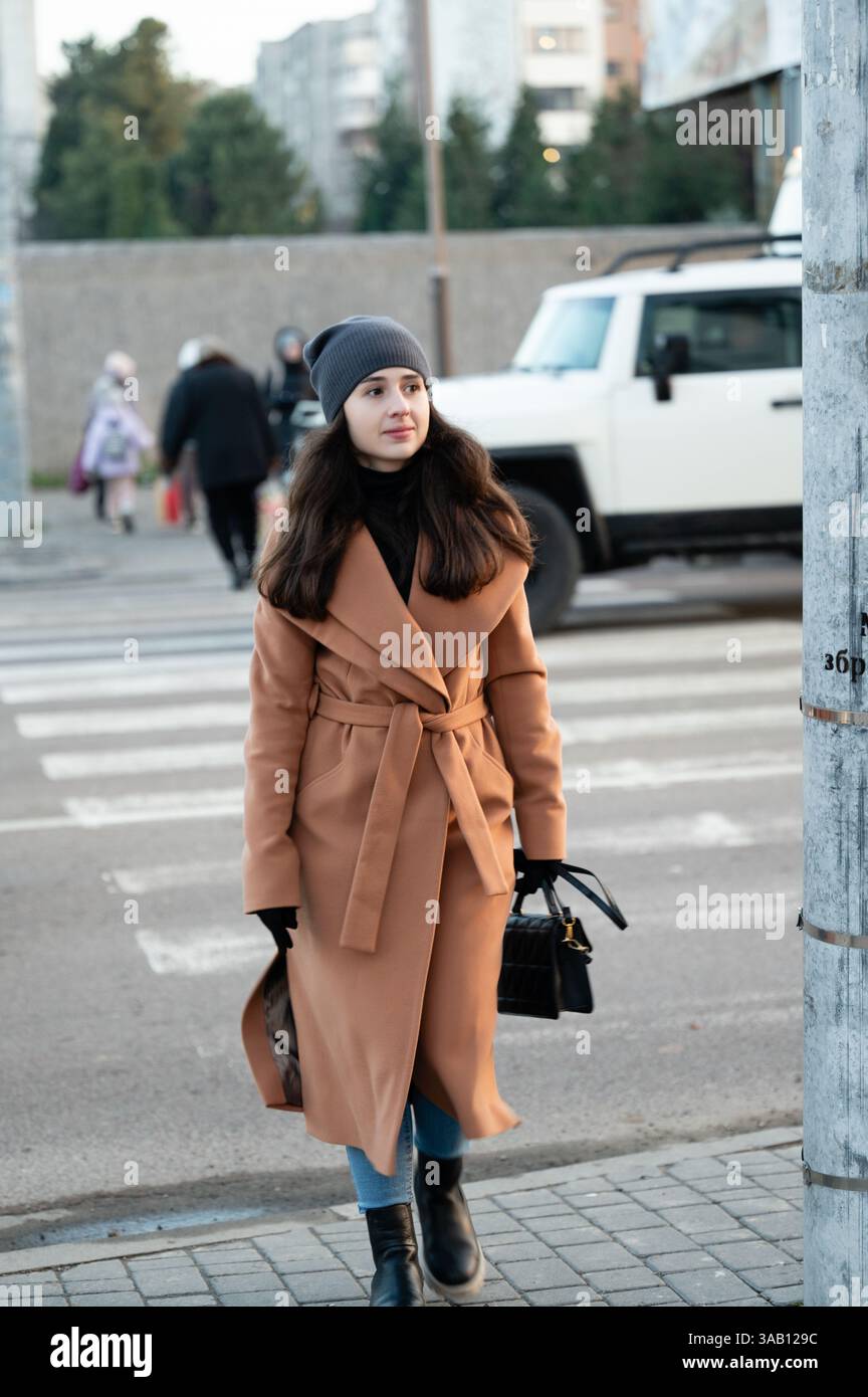 A young woman walks confidently across a crosswalk in a stylish coat ...