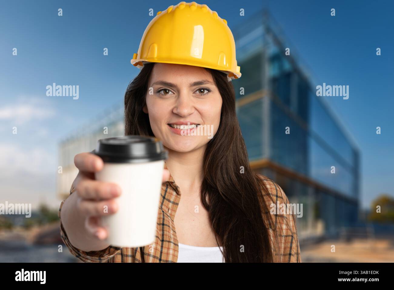 A smiling female construction worker wearing a yellow hard hat extends a takeaway coffee cup ...