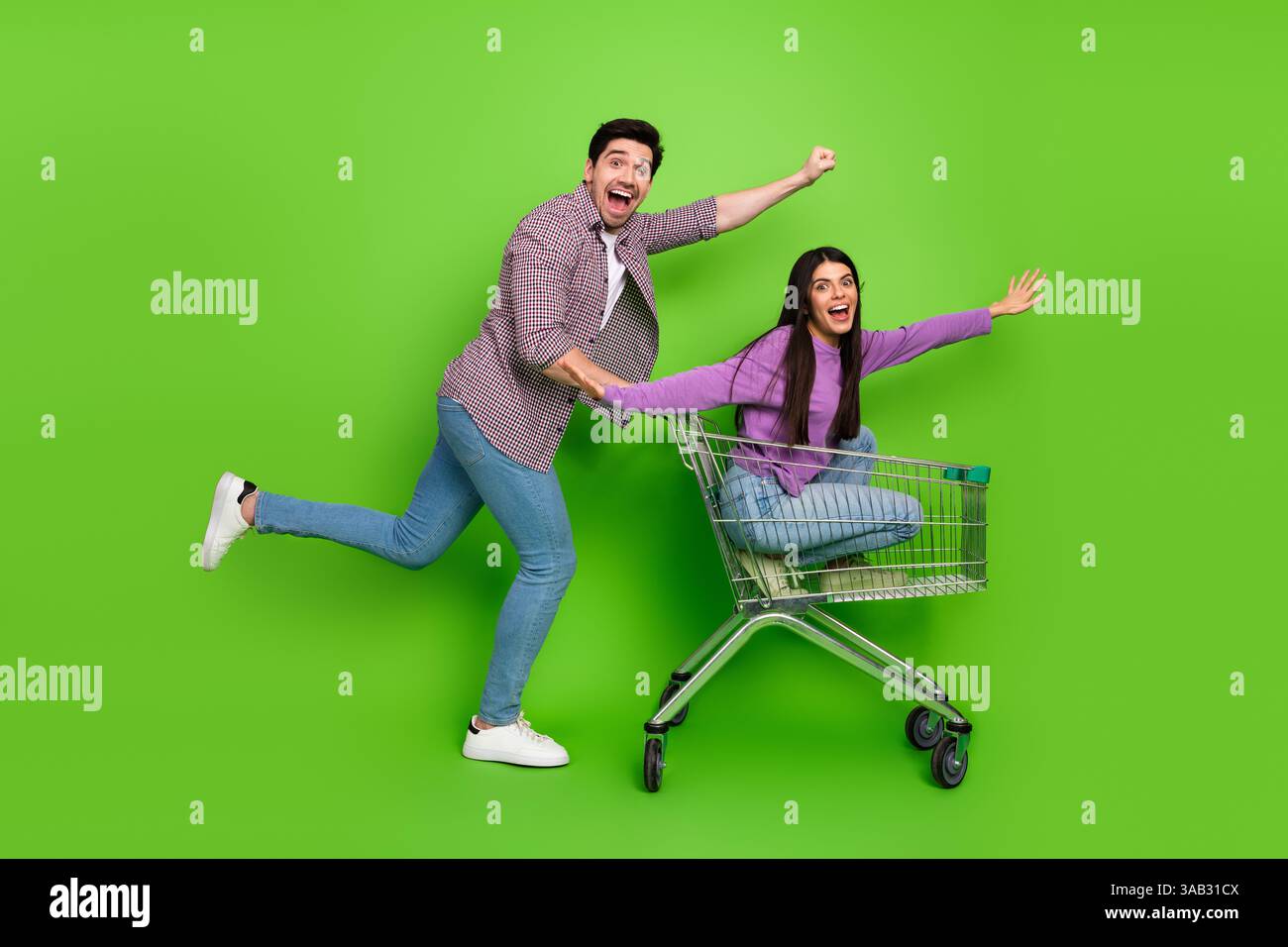 Happy young couple having fun with a shopping cart on a vibrant green ...