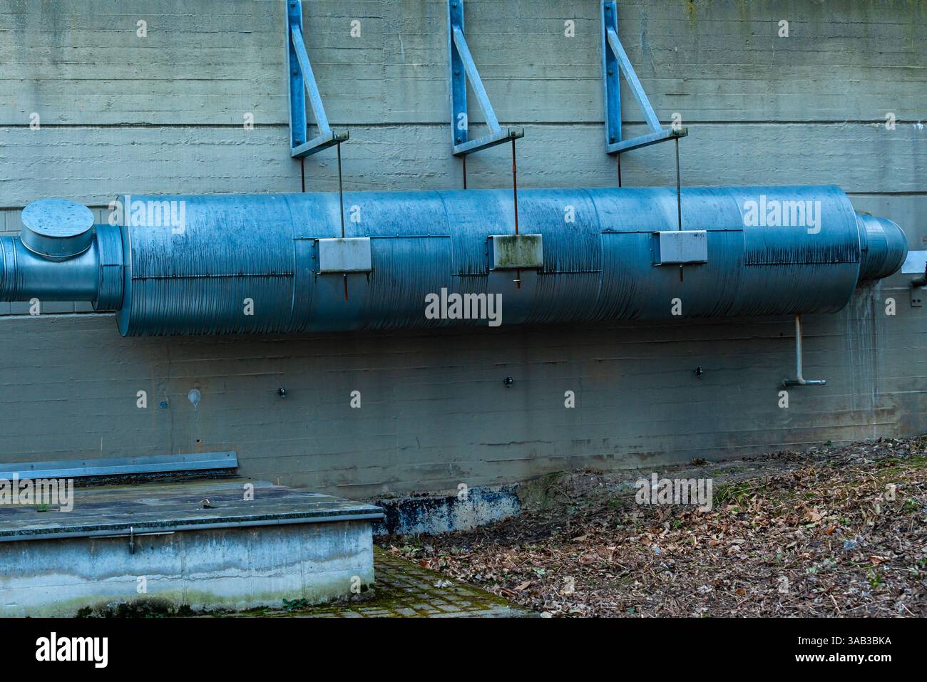 A large metallic pipe structure is mounted on a concrete wall ...