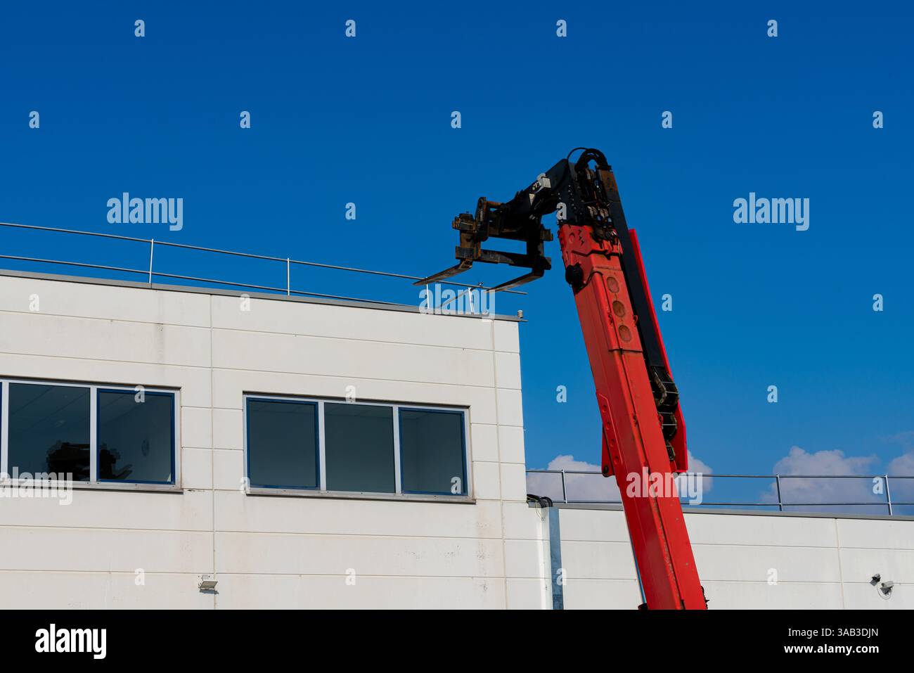 A red forklift extends its arm towards the upper section of a modern ...