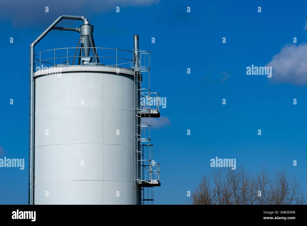 A large cylindrical storage tank stands prominently against a bright ...