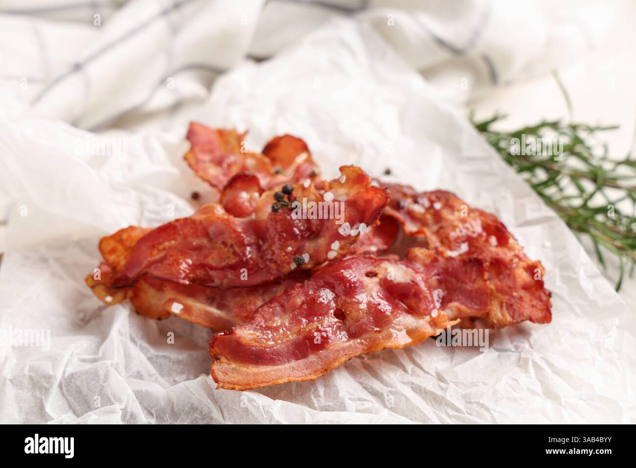Baking paper with fried bacon rashers and peppercorn on white ...