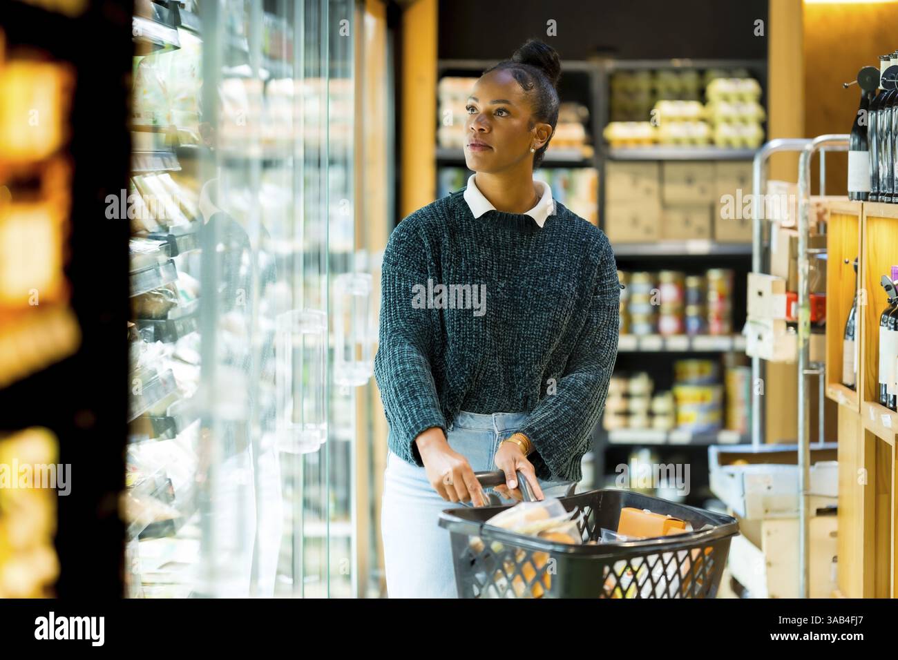 Young woman pushing shopping basket and choosing groceries while ...