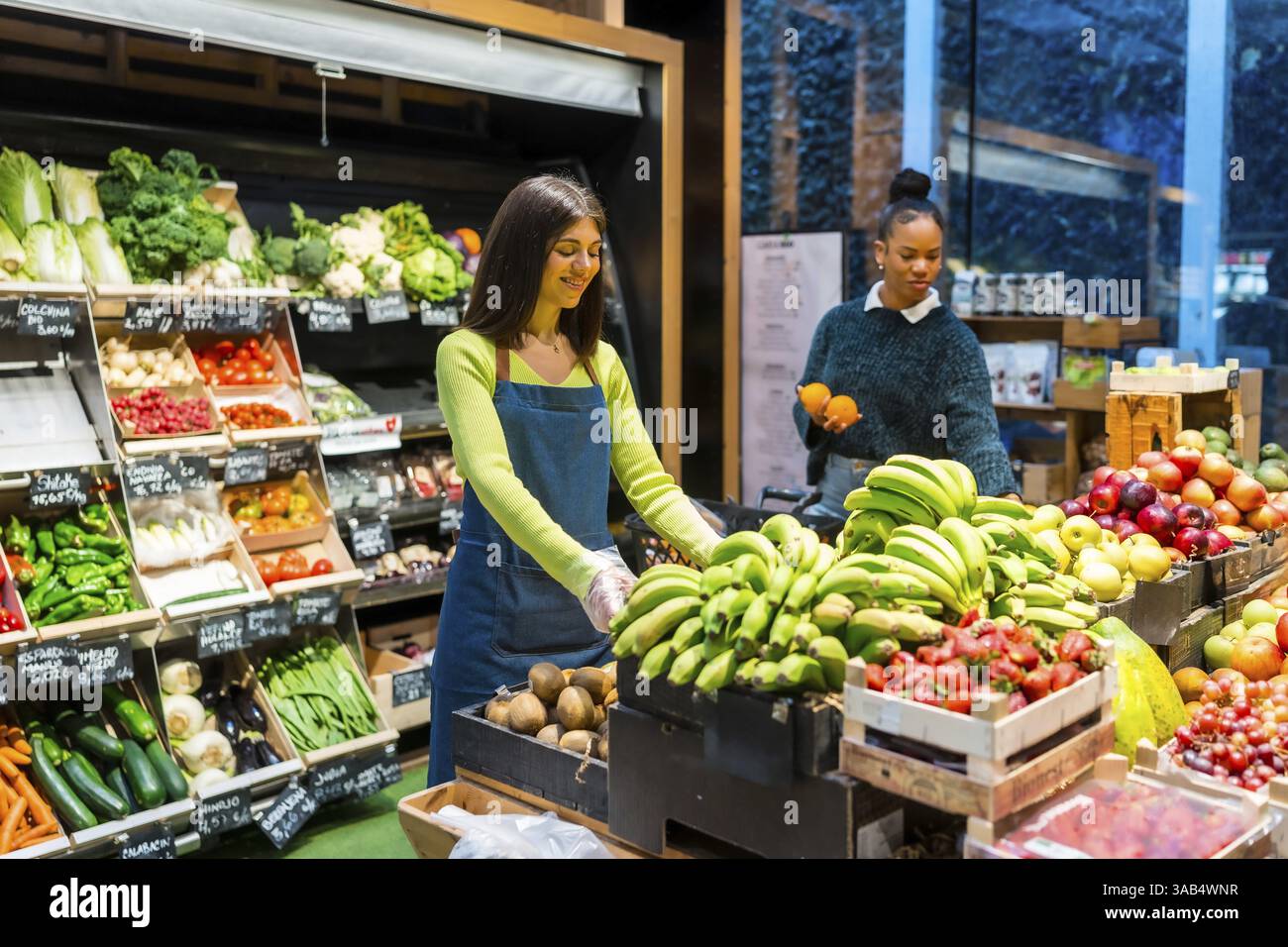 Supermarket employee organizing fresh fruits and vegetables, assisting ...