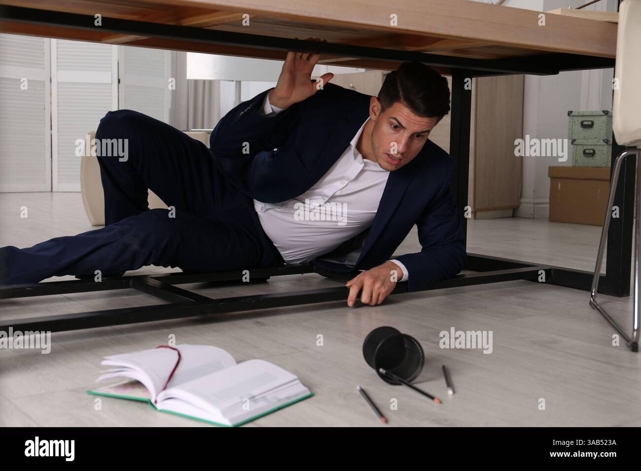 Scared man hiding under office desk during earthquake Stock Photo - Alamy