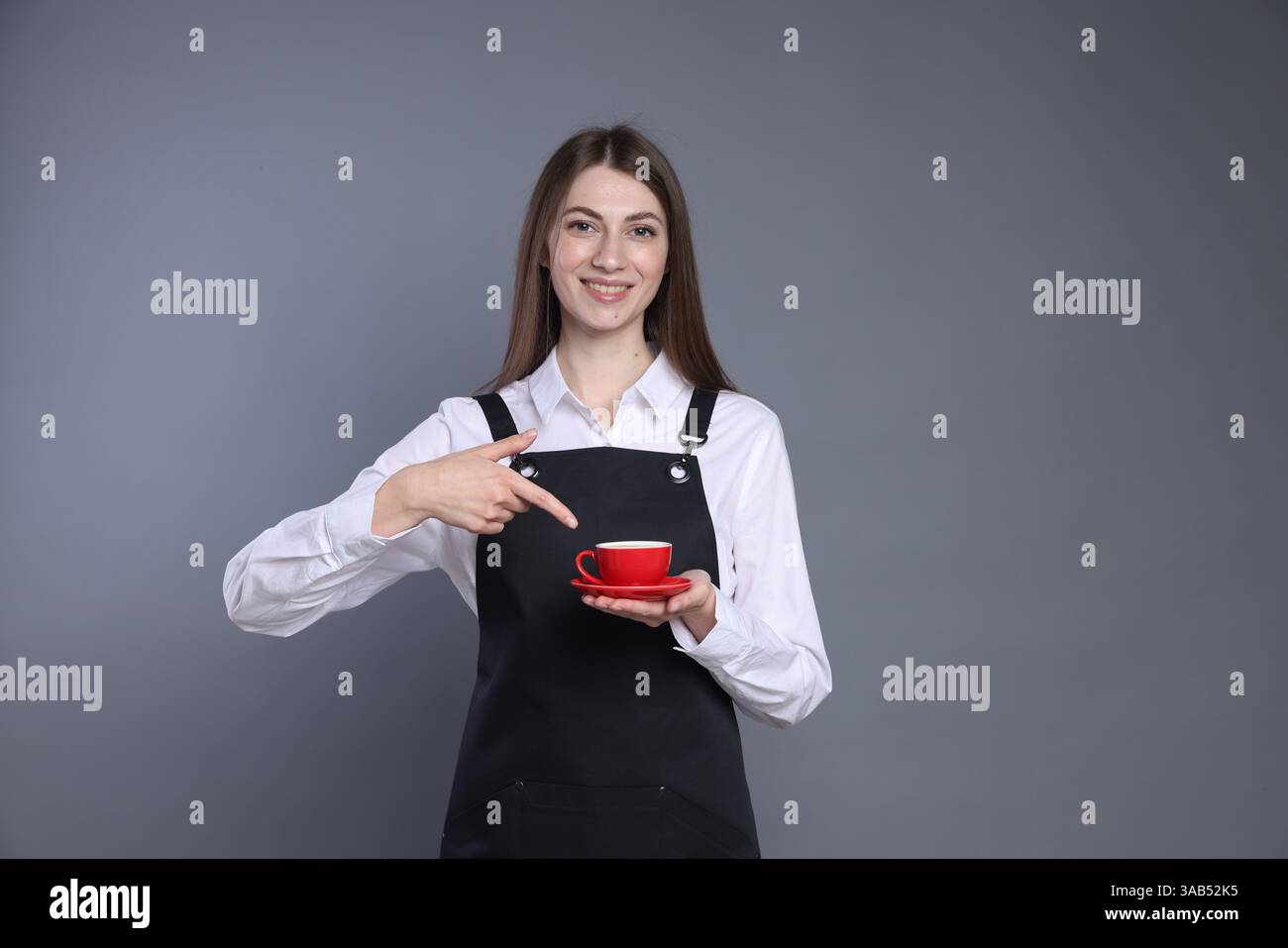 Portrait of smiling barista pointing at cup of hot drink on grey ...