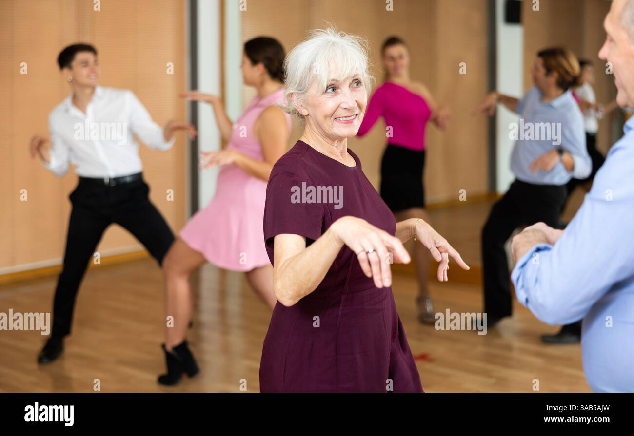 Cheerful elderly female dancer practicing ballroom dances in ballroom ...