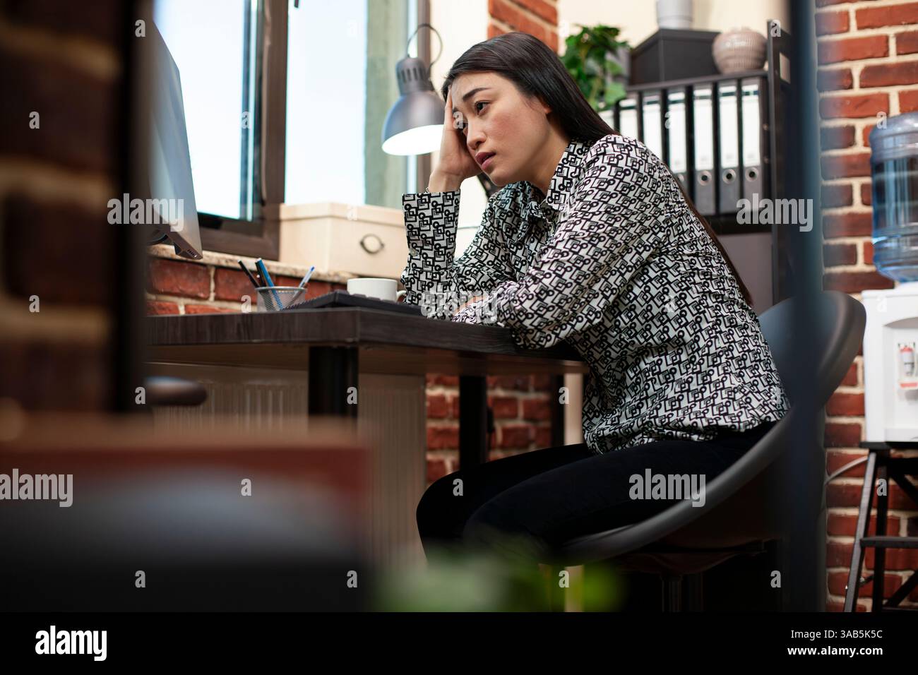 Exhausted female employee seated at desk with computer, visibly tired ...
