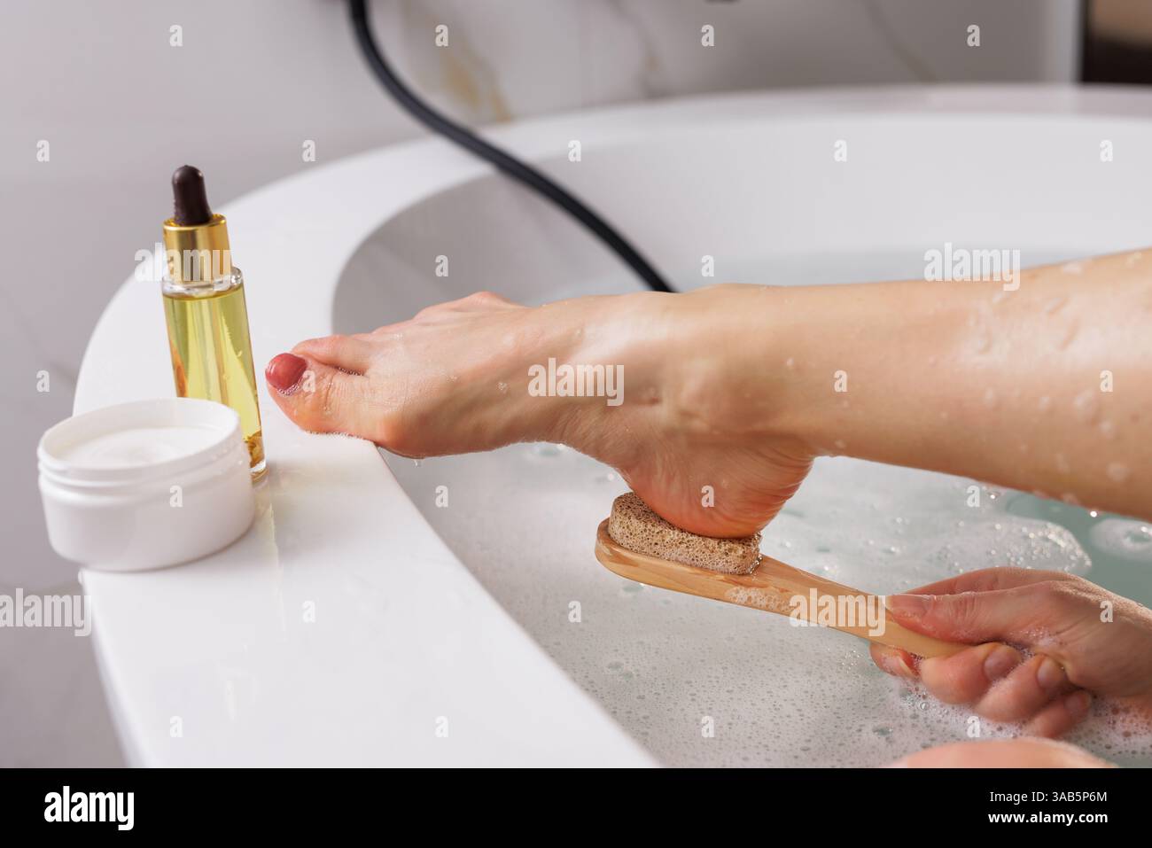 Woman exfoliating foot with pumice stone in bathtub, luxurious spa ...