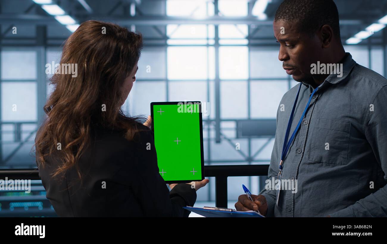 Engineers using green screen tablet in data center, checking infrastructure reliability, writing ...