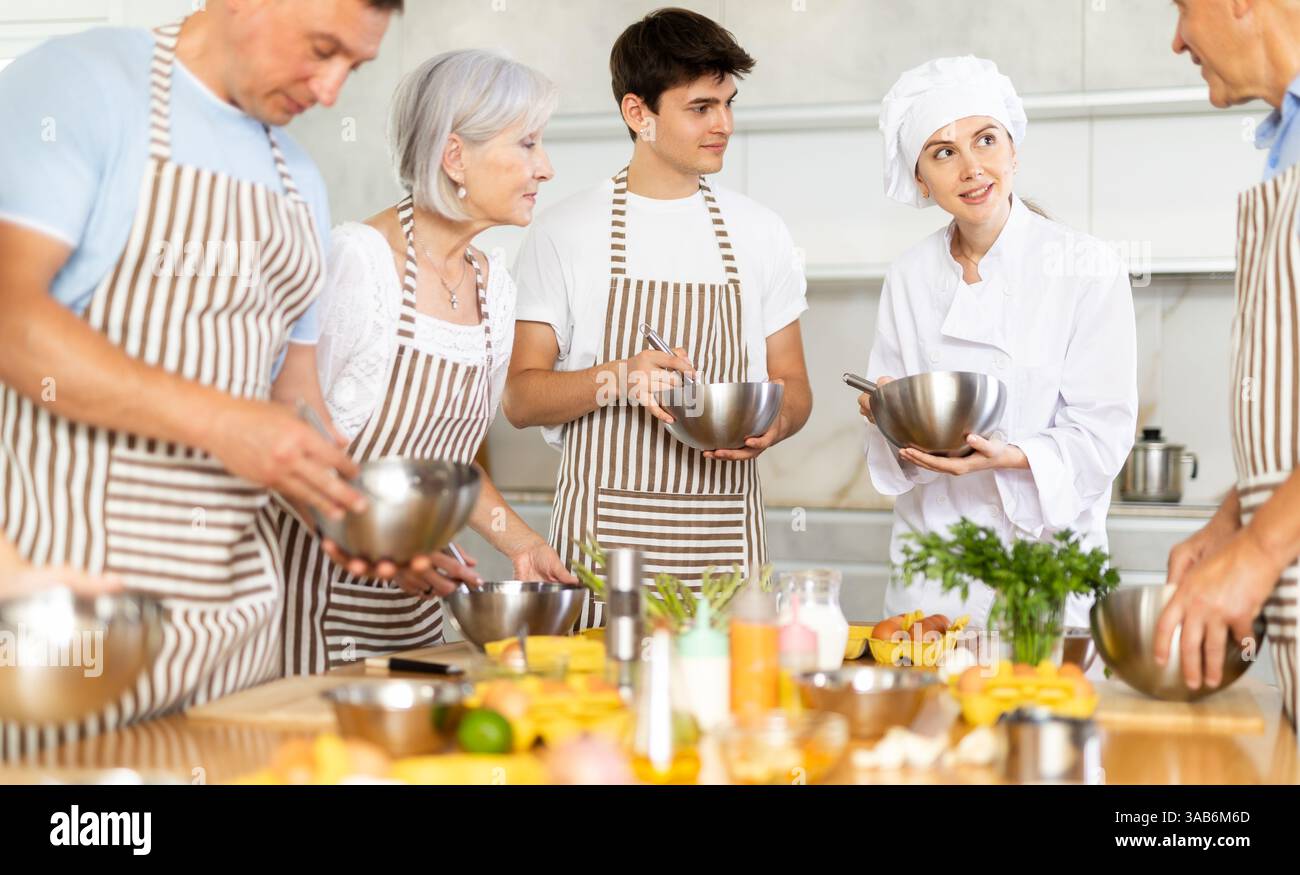 Female chef giving instructions to students standing around table in ...