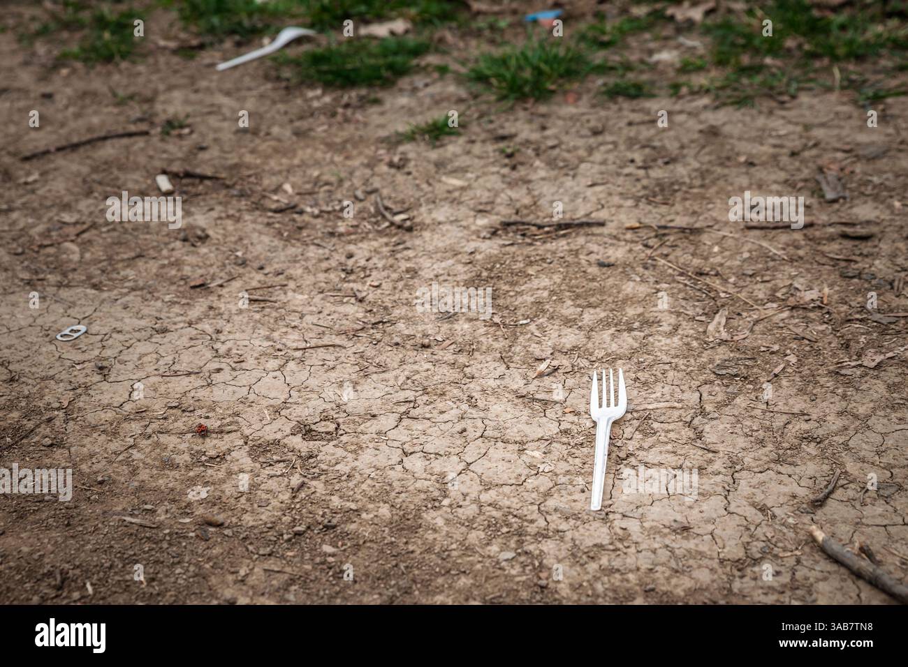 Single-use plastic fork discarded as litter and garbage on cracked soil ...