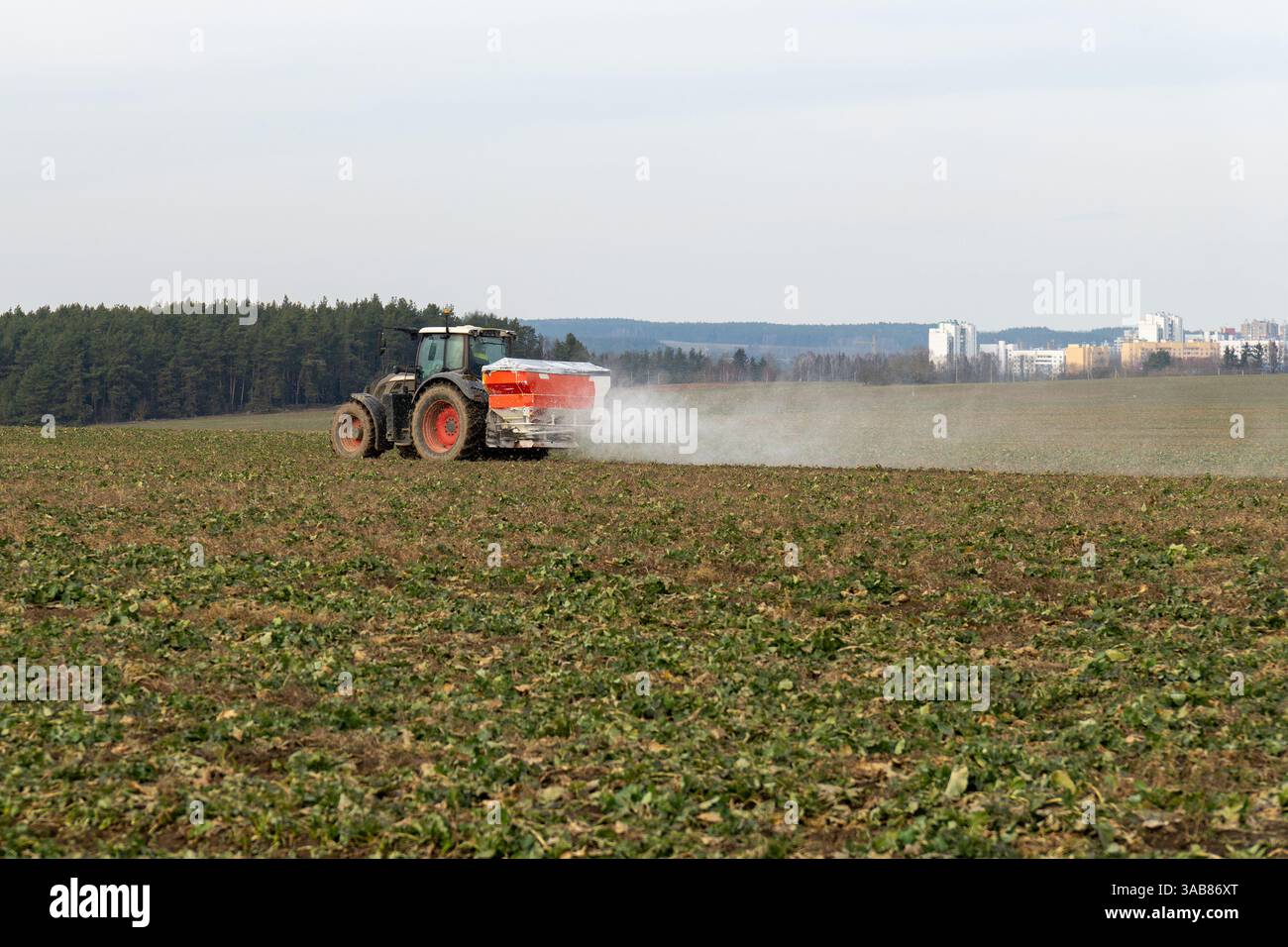 A tractor towing a mineral fertilizer dispenser across a green field ...