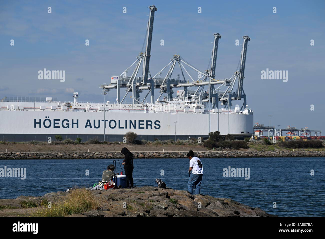 People are seen fishing in front of a Hoegh Autoliner ship docked at ...