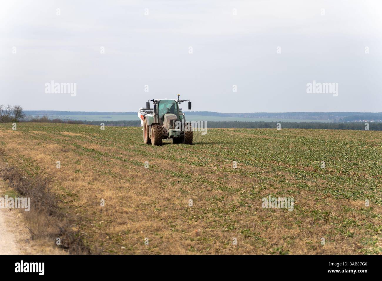 A tractor towing a mineral fertilizer dispenser across a green field ...
