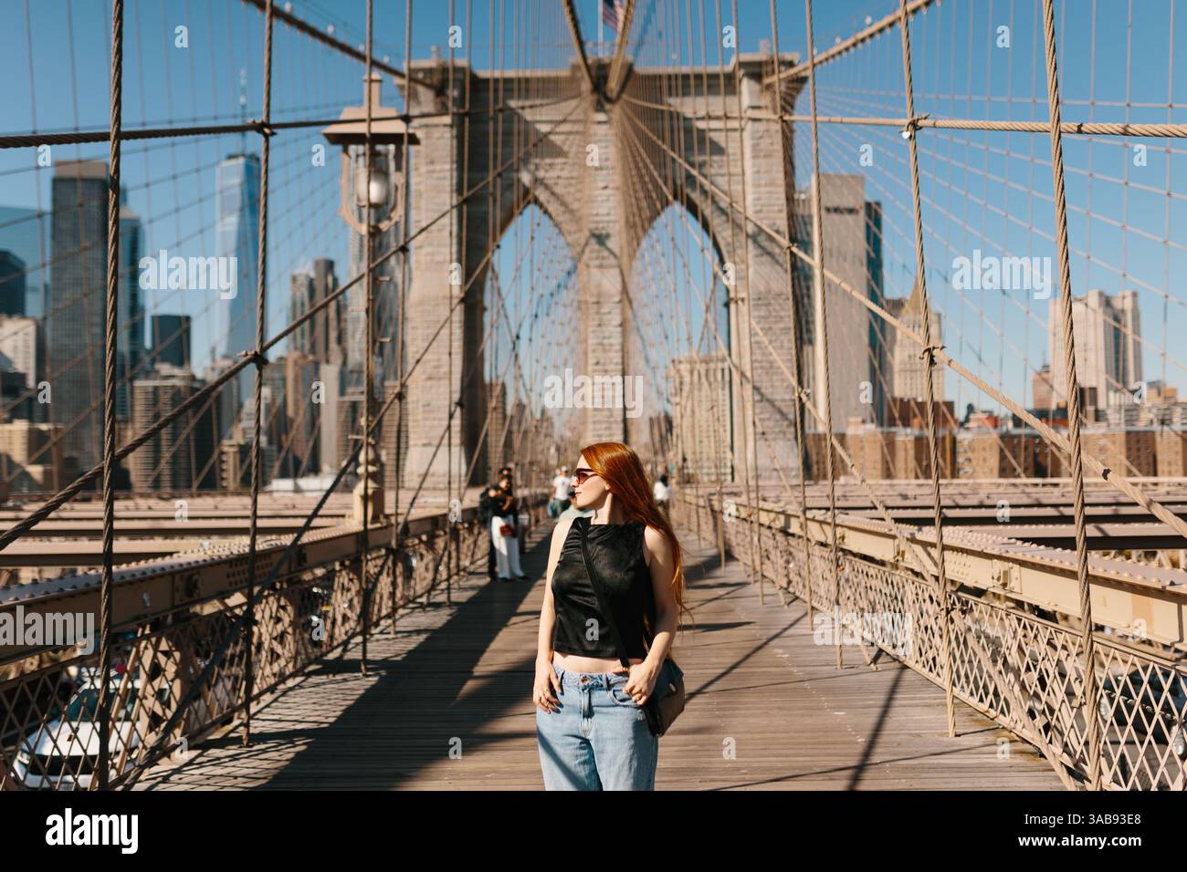 A woman with red hair walks across the Brooklyn Bridge, basking in the ...