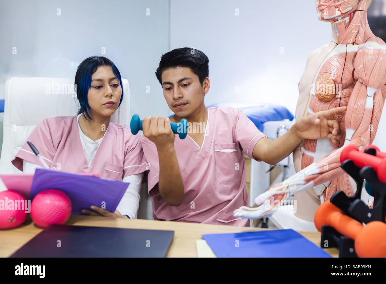 Two physiotherapy students in an Ecuador clinic study anatomy with a muscular model and weights ...