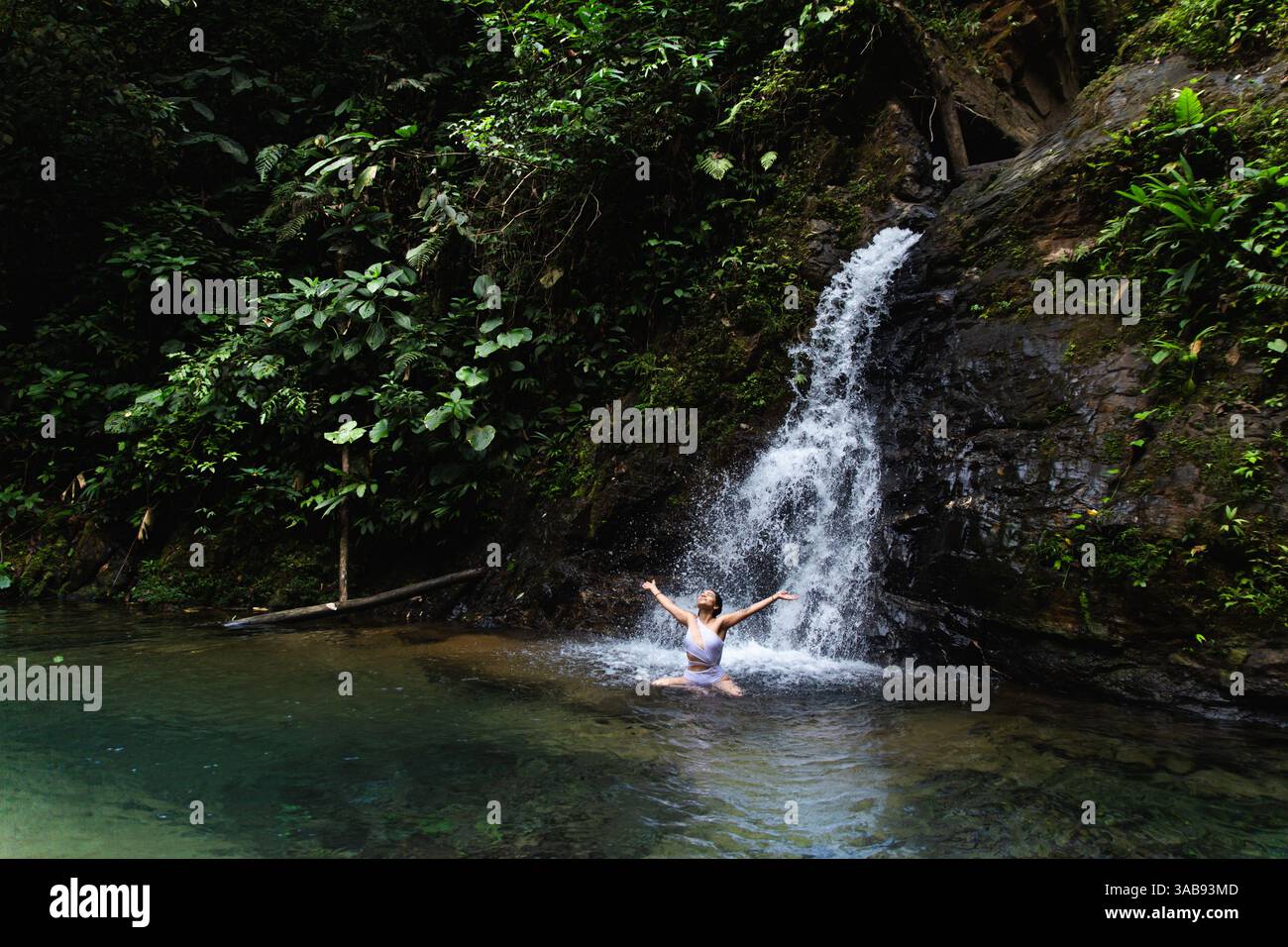 Young woman enjoying and stretching arms in a natural pool under a ...