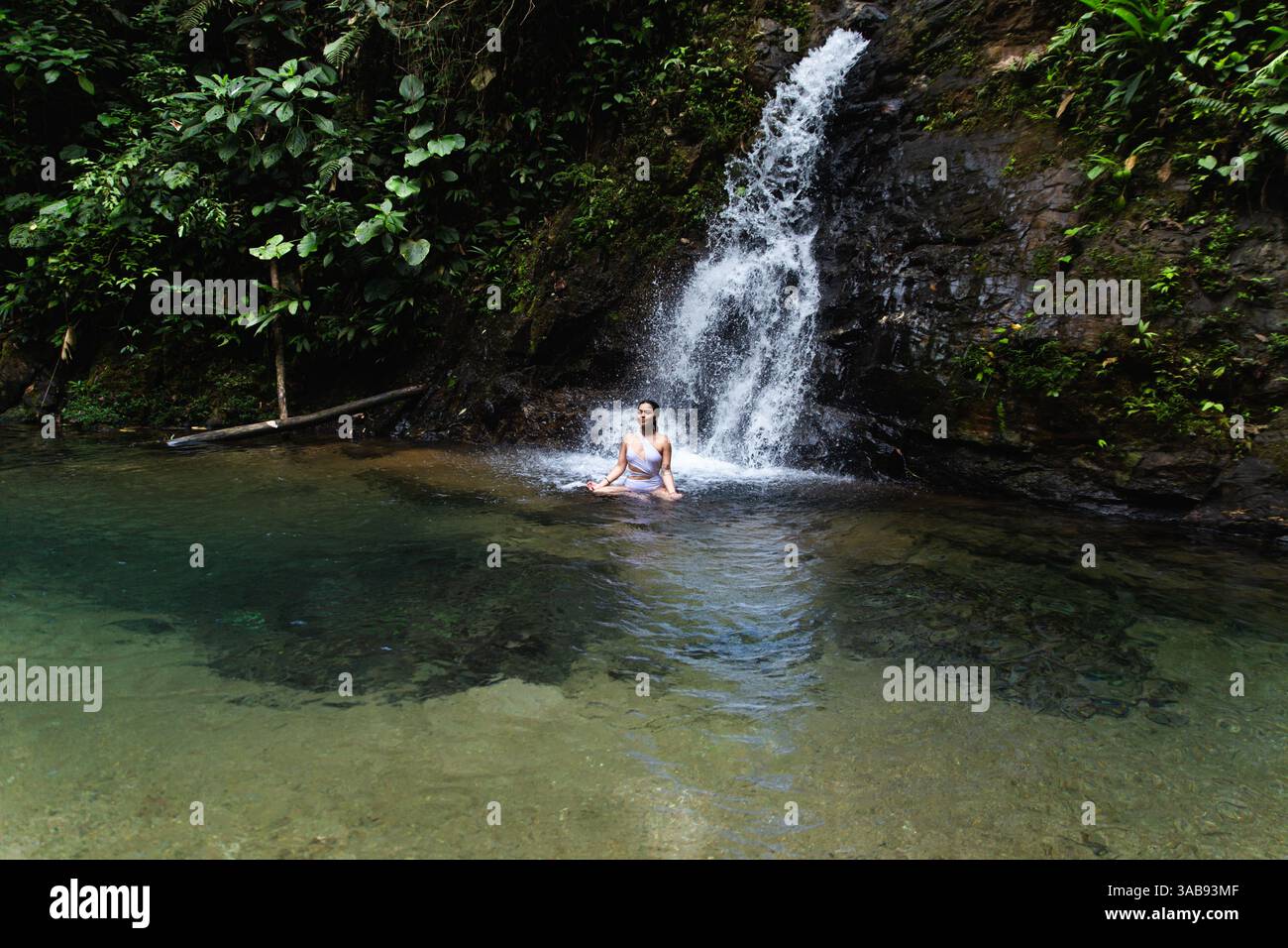 A young woman meditates under a lush waterfall in the biodiverse Choco ...