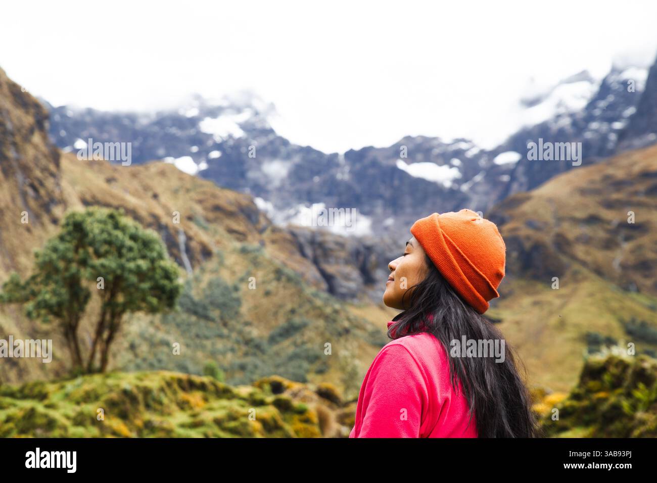 An Ecuadorian woman in a bright orange hat and pink jacket gazes at the majestic El Altar ...