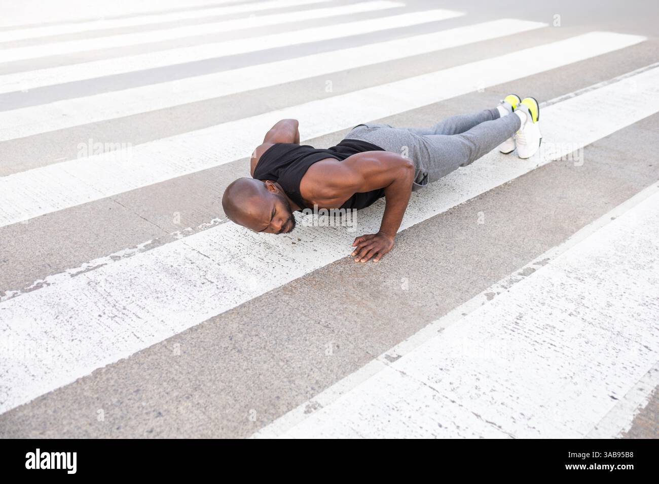 A fitness cuban man performs push ups on a city crosswalk, showcasing ...