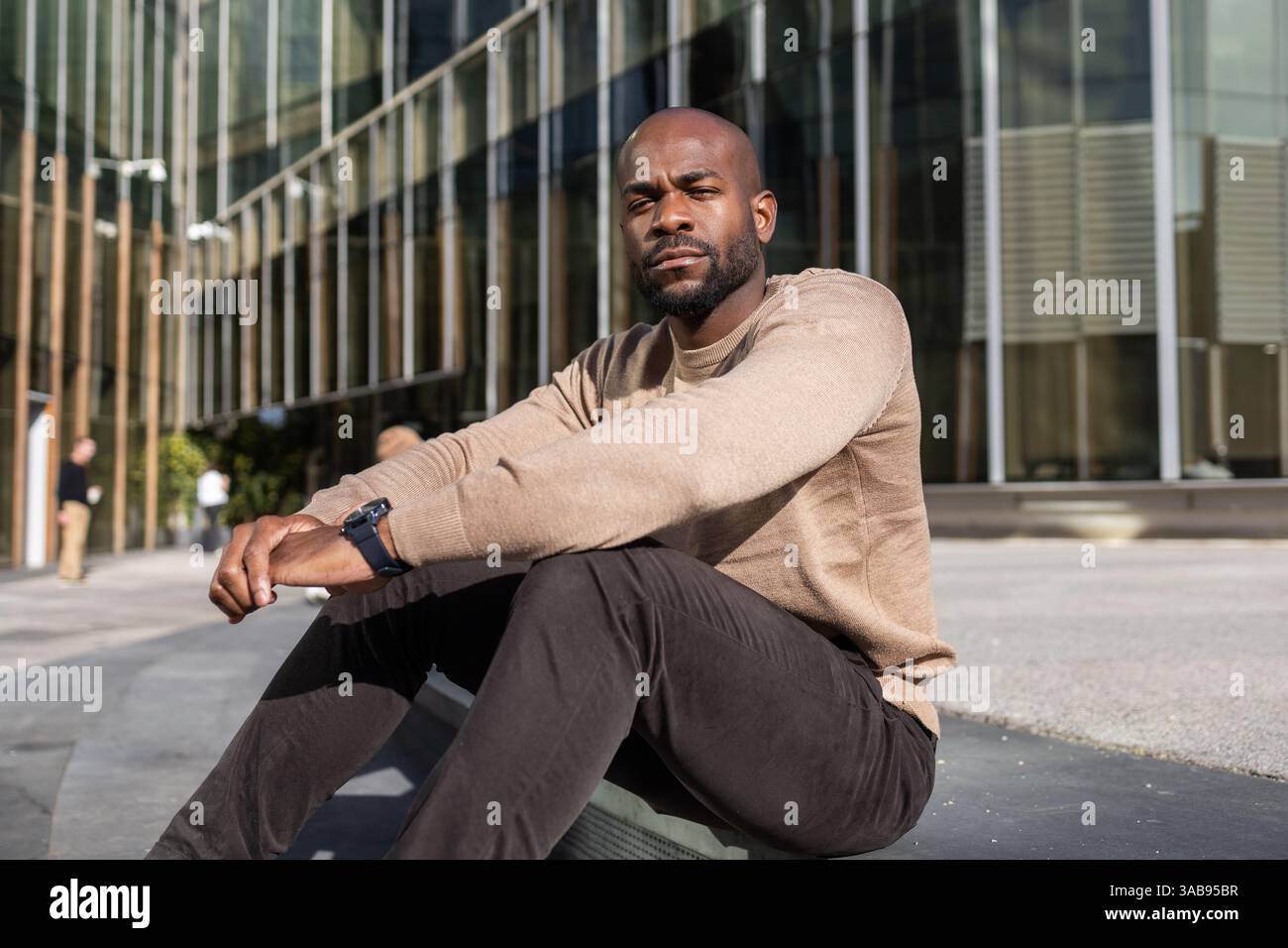 A cuban man in casual attire sits outside a modern glass building ...