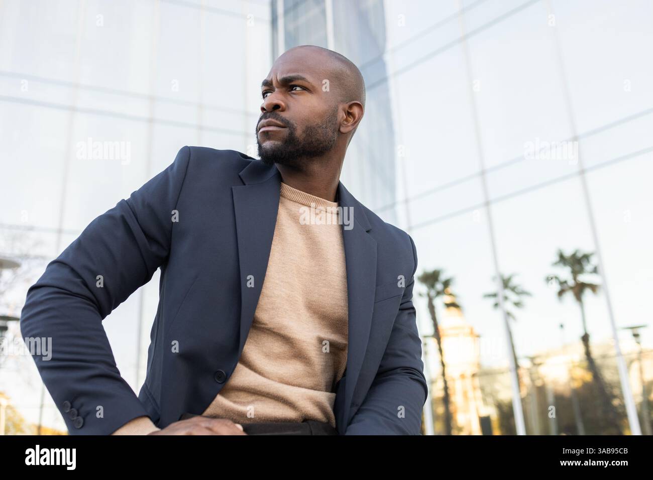 A confident business cuban man in a blazer poses outside a modern glass ...