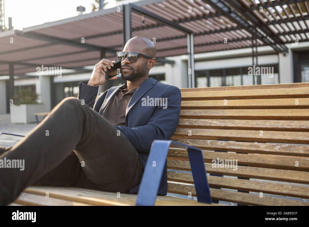 A business cuban man in a suit and sunglasses sits relaxed on a wooden ...
