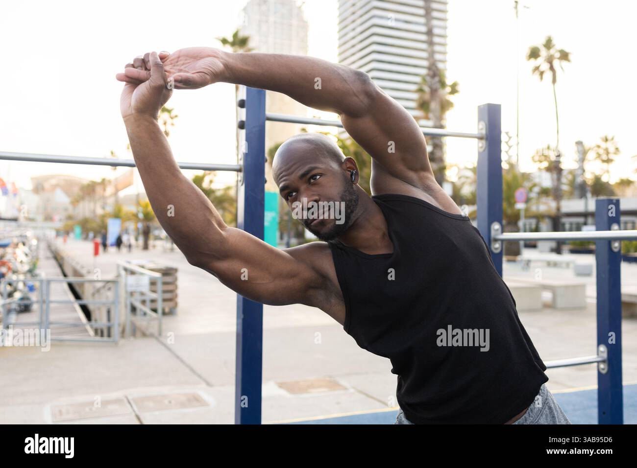 A cuban man in a black tank top performs a stretching exercise outdoors ...